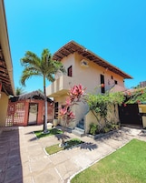 Um edifício de dois andares com telhado em telhas, um pequeno alpendre e um portão vermelho.