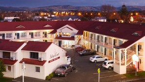 Um hotel com vários andares, teto vermelho, placa indicando motel com spa e estacionamento com vários carros.