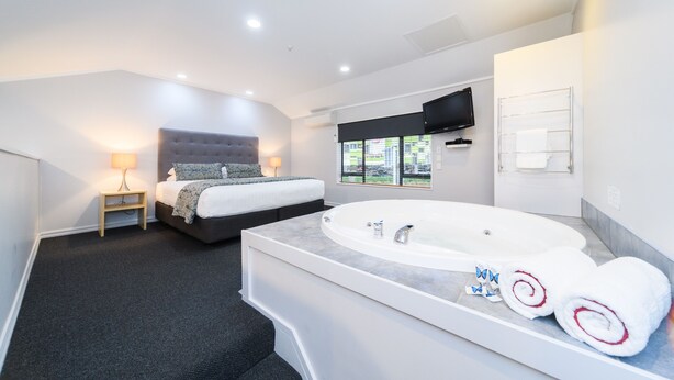 Quarto de hotel moderno com uma cama grande, um espaço de estar separado, uma banheira e uma TV montada na parede.