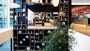 Um interior moderno com uma área de estar central, rodeada por estantes com objetos decorativos e uma grande planta em vaso.