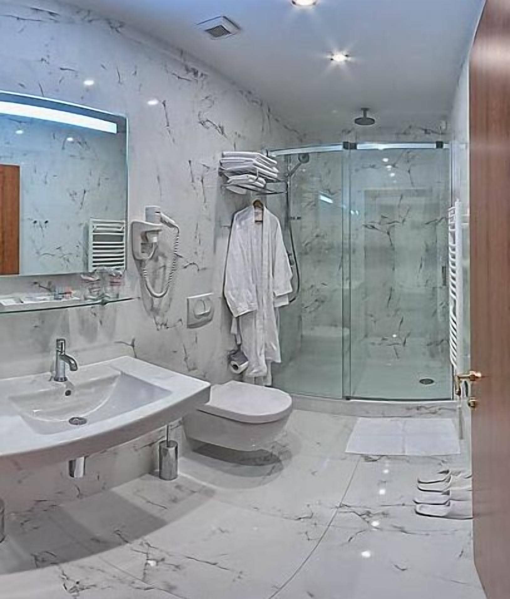 Uma casa de banho moderna com lavatório de mármore, sanita, cabine de duche em vidro e um porta-toalhas.