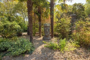 Um jardim com uma estátua de pedra, cercado por diversas plantas e árvores.