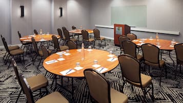 Uma sala de conferências com várias mesas e cadeiras, um quadro branco e uma tela de projeção.