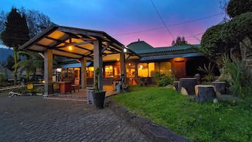 Um edifício com área de estar coberta ao ar livre, entrada pavimentada e paisagem ajardinada.