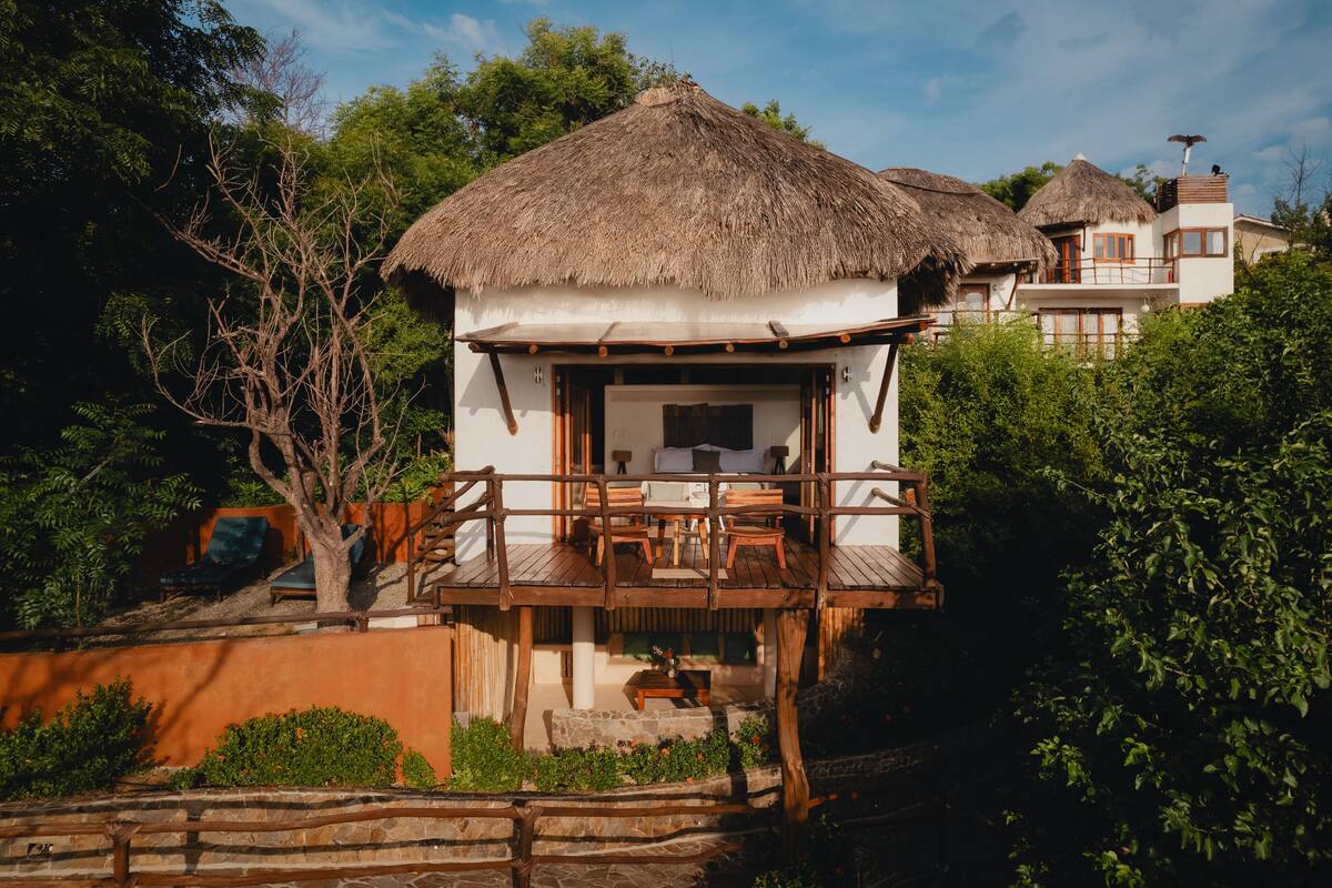 Uma cabana com telhado de palha, deck de madeira e uma pequena varanda.