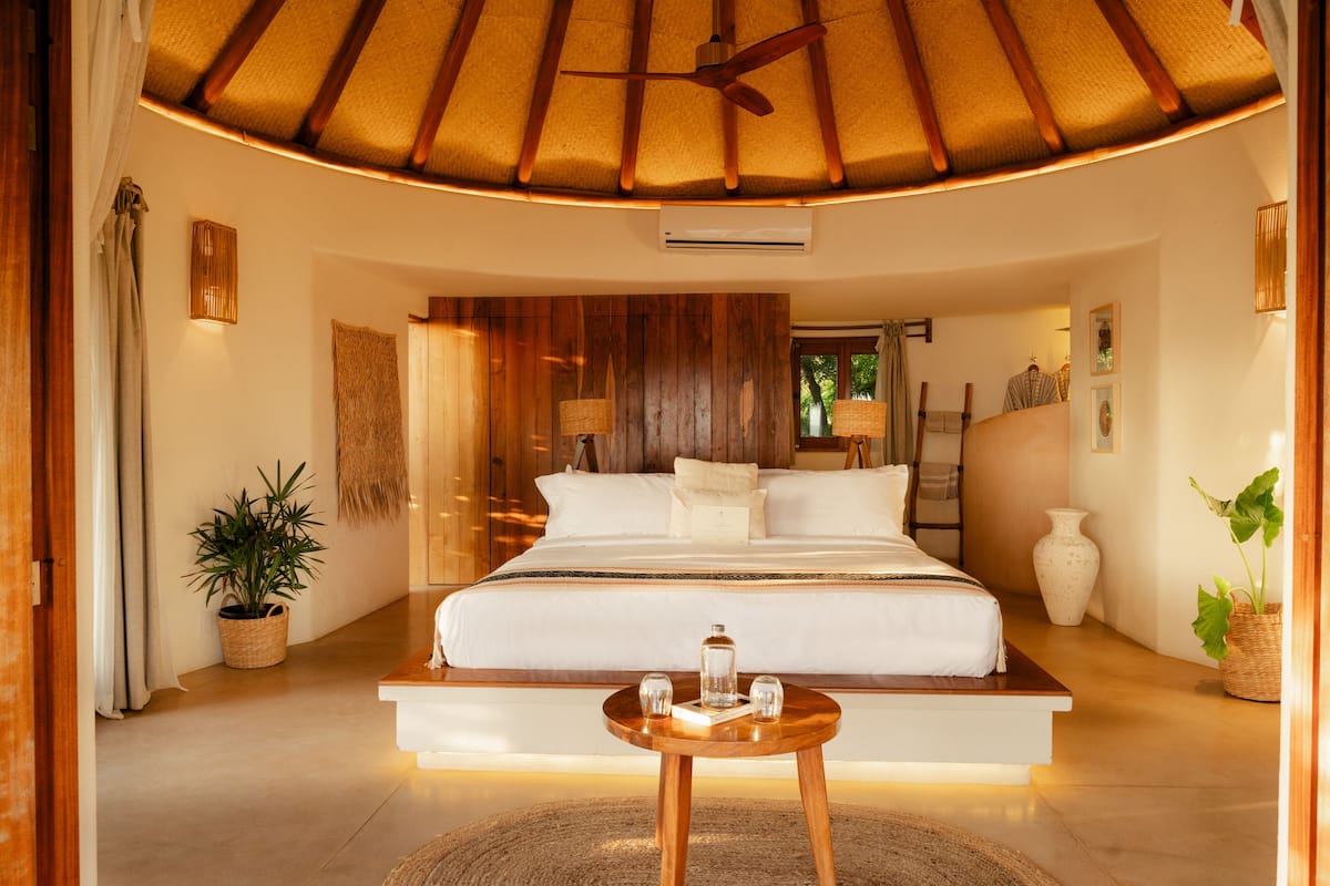 Quarto moderno com uma cama grande, teto de madeira e uma mesinha com copos.