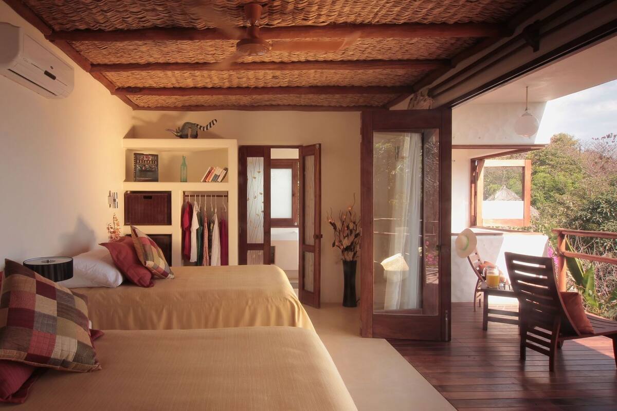 Quarto com cama, almofadas, guarda-roupa, espelho e varanda com mesa e cadeiras.