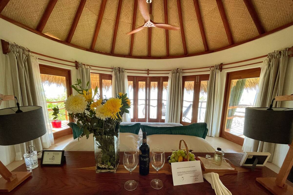 Quarto com teto de madeira, mesa de jantar com um vaso de flores, copos de vinho e um menu.
