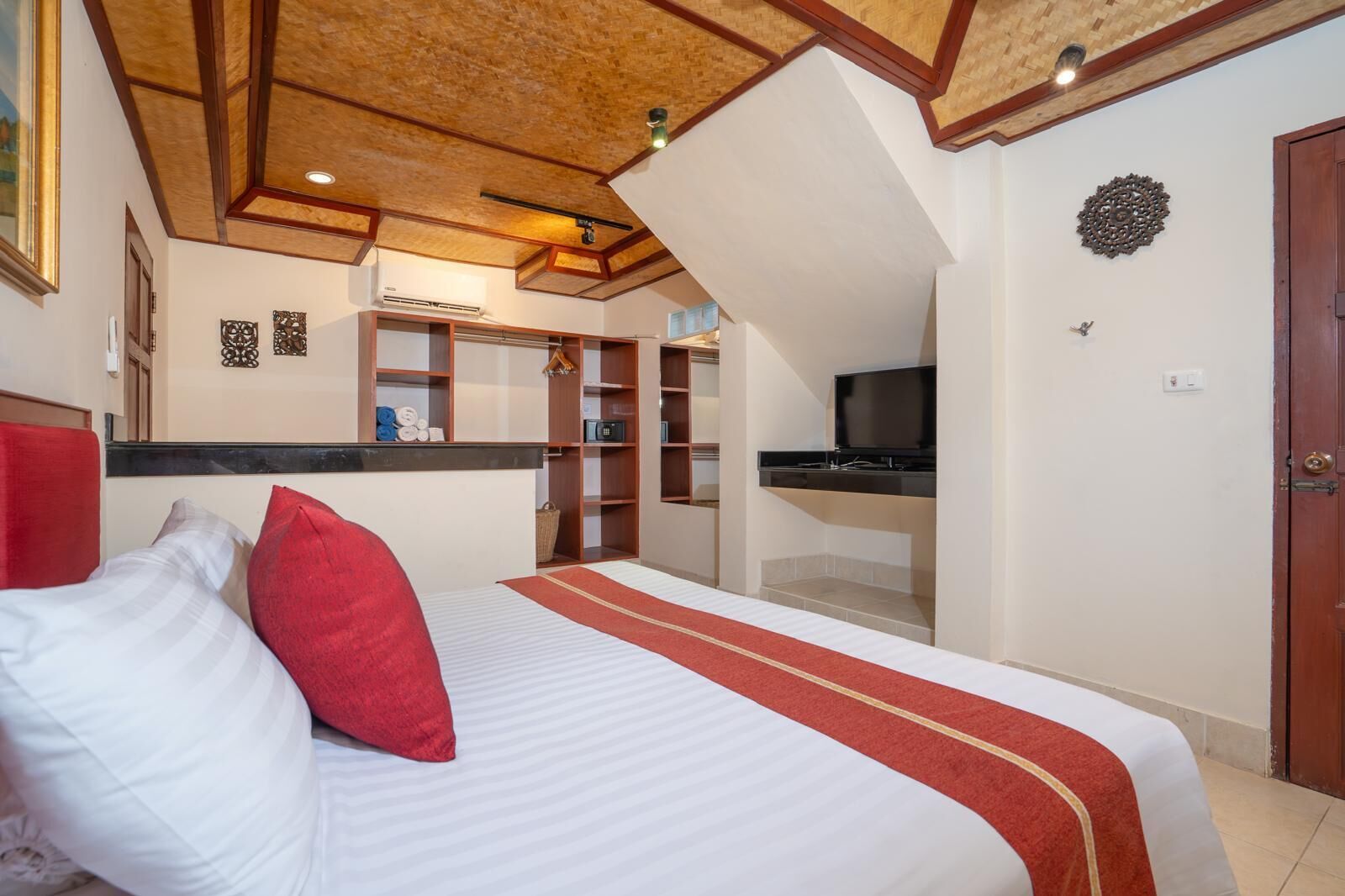 Quarto de hotel com cama, televisão, guarda-roupa e uma pequena cozinha equipada.