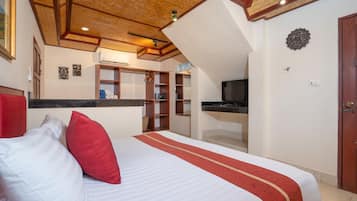 Quarto de hotel com cama, televisão, guarda-roupa e uma pequena cozinha equipada.