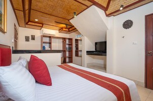 Quarto de hotel com cama, televisão, guarda-roupa e uma pequena cozinha equipada.