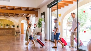Um hall com piso de azulejos, vigas de madeira no teto, um balcão de recepção e uma porta de vidro que dá para o exterior.