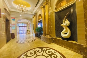 Um hall de hotel com um lustre imponente, uma grande peça decorativa na parede e um design de piso estampado.