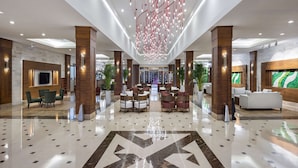 Um hall amplo com piso de mármore polido, uma área de estar central com várias cadeiras e um lustre moderno.