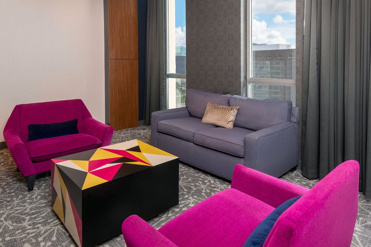 Uma sala de estar moderna com um sofá cinzento, uma poltrona rosa e uma mesa de centro preta com padrão geométrico.