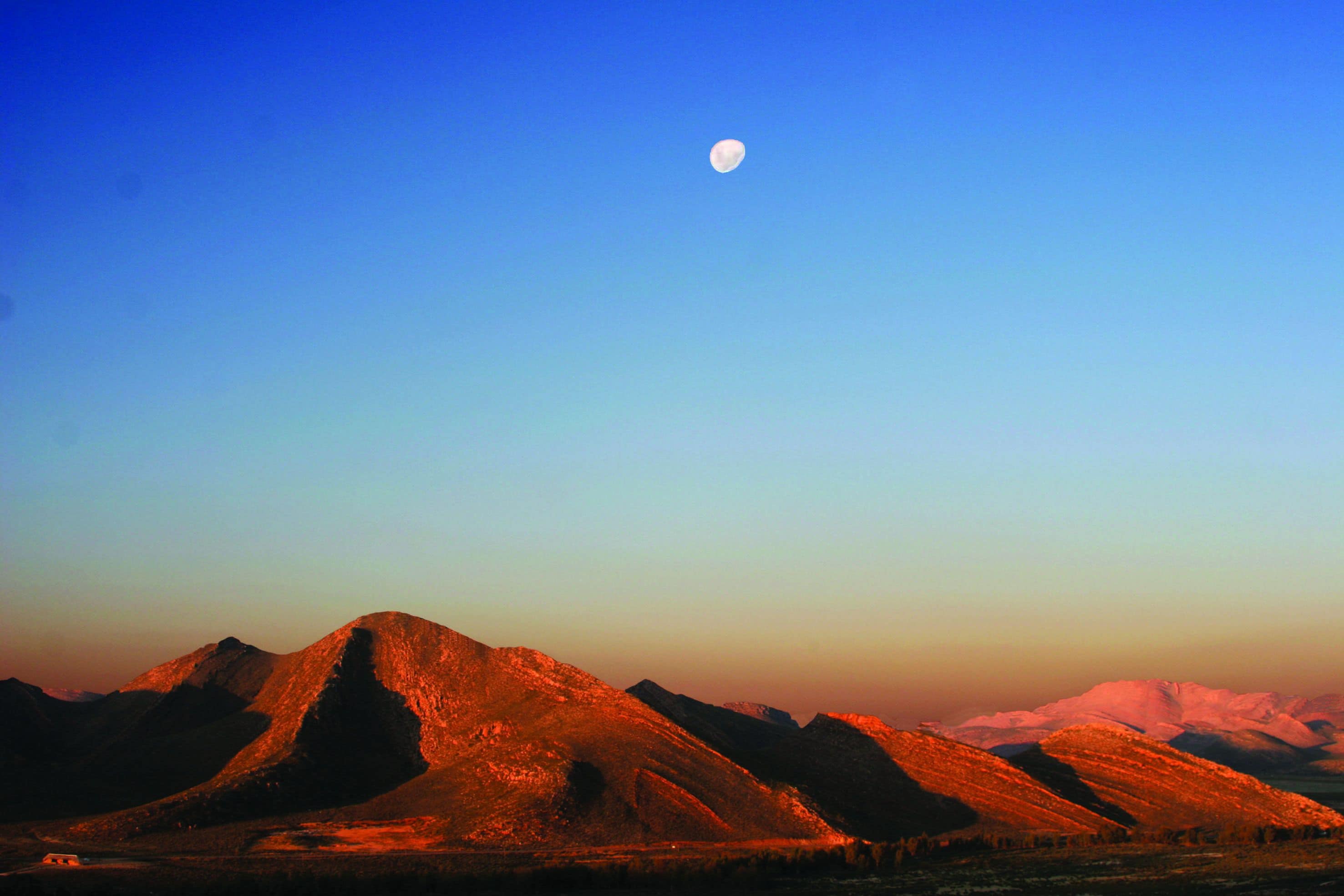 Paisagem montanhosa com uma lua cheia no céu.