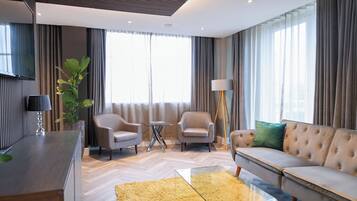 Uma sala de estar moderna com um sofá, poltronas, uma mesa de centro e uma TV fixada na parede.