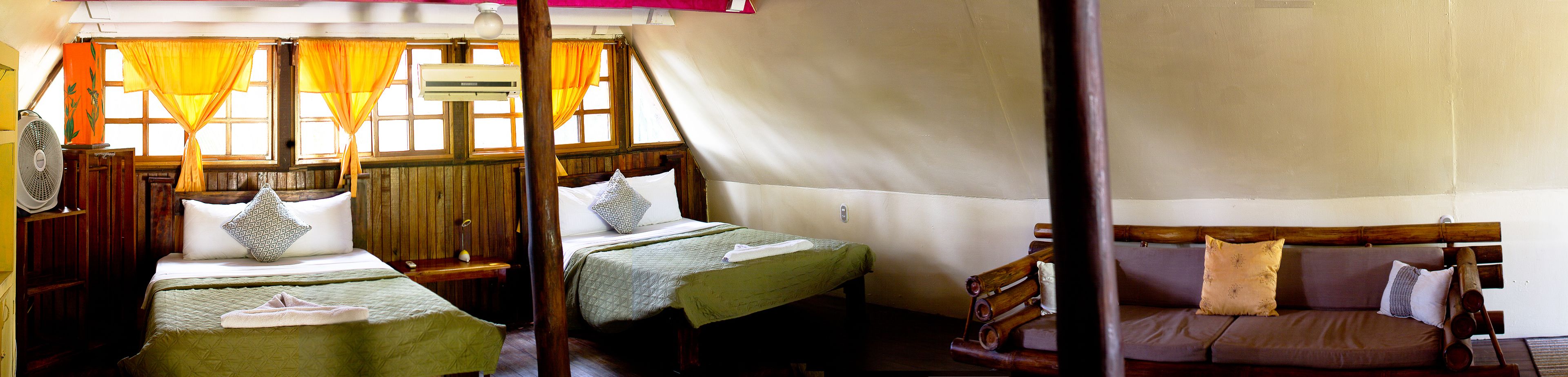 Quarto com duas camas, cabeceira de madeira, um ventilador e uma janela com cortinas.