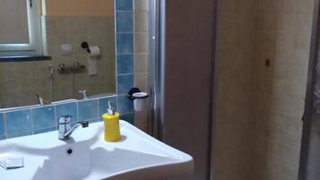 Uma casa de banho com uma pia branca, um espelho, um chuveiro e uma porta.