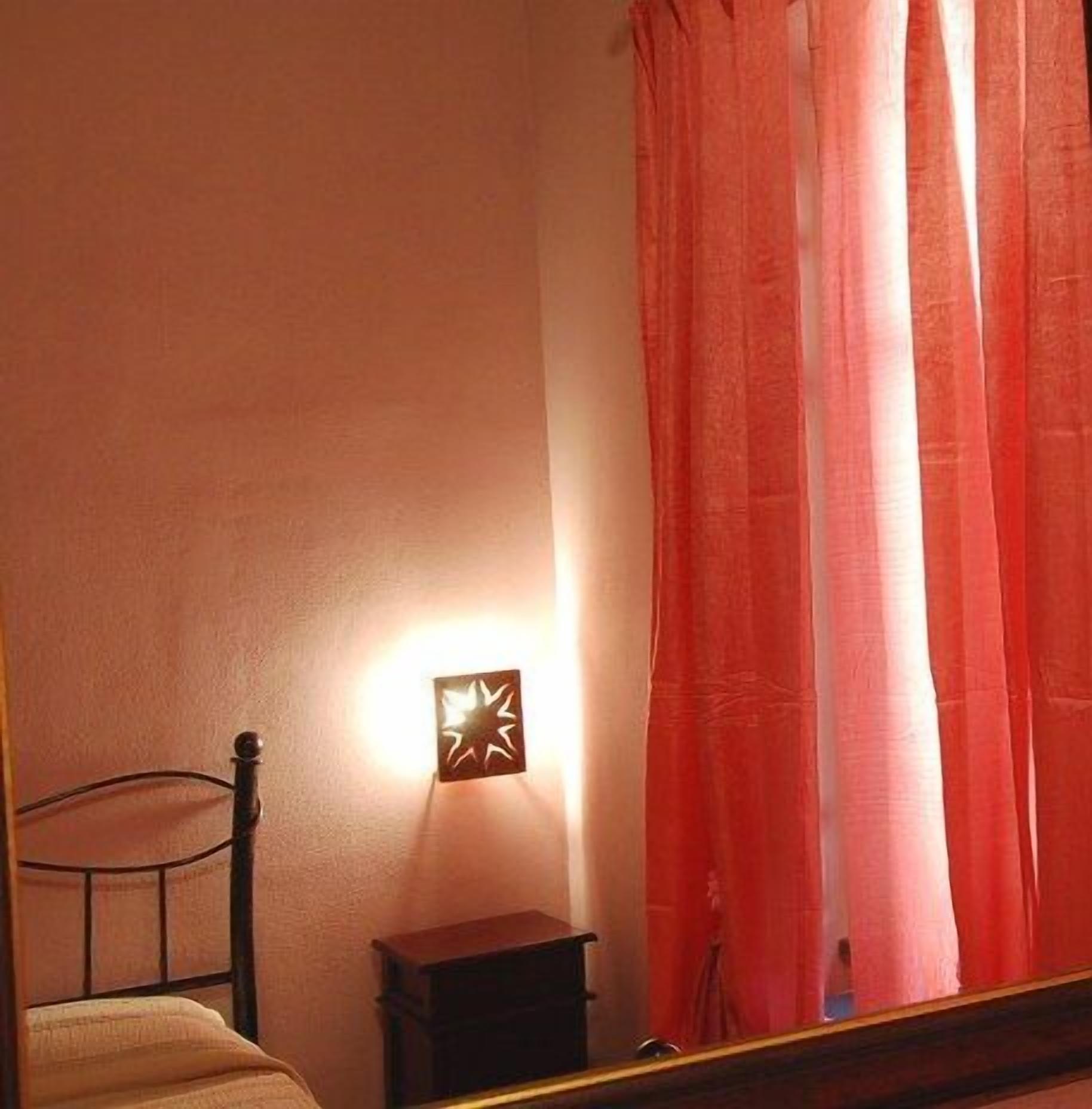 Um quarto com uma cama, uma mesinha de cabeceira, um relógio de parede e uma janela com cortinas.