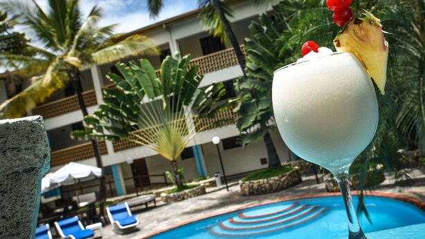 Um copo de bebida branca com abacaxi e frutas vermelhas sobre uma mesa à beira da piscina.