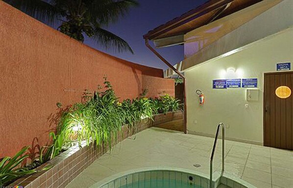 Área de piscina externa com piso ladrilhado, porta de madeira e placa indicando uma sauna.