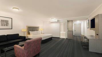 Quarto de hotel com cama, escrivaninha, poltrona, sofá e televisão.