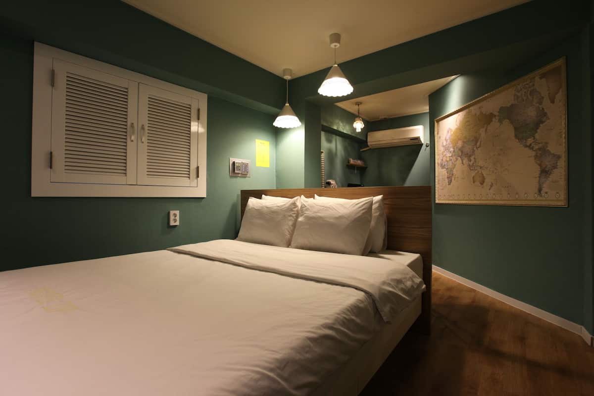 Quarto com uma cama, um mapa na parede e uma janela com persianas.