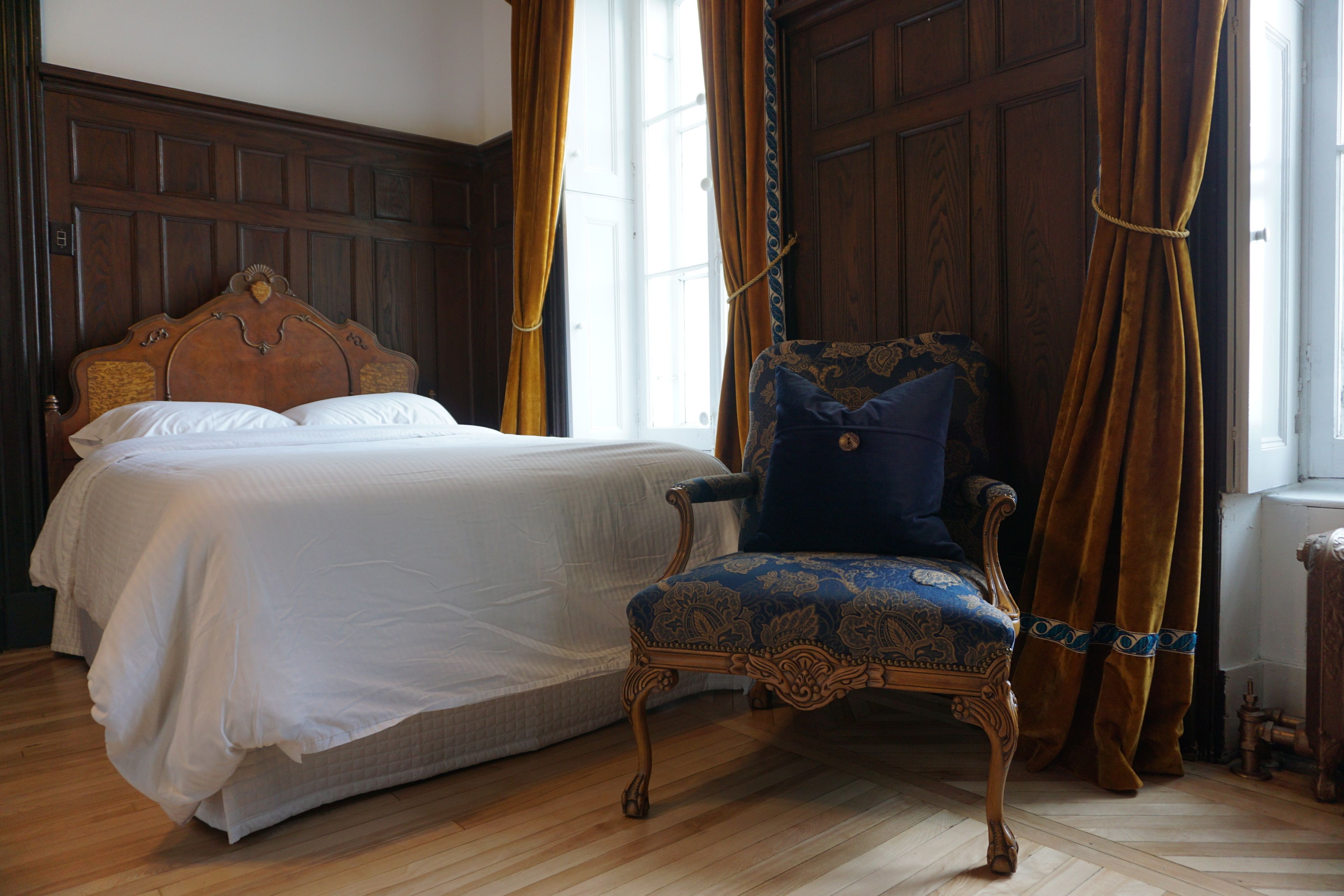 Quarto com uma cama grande, cabeceira de madeira e uma cadeira com tecido estampado.