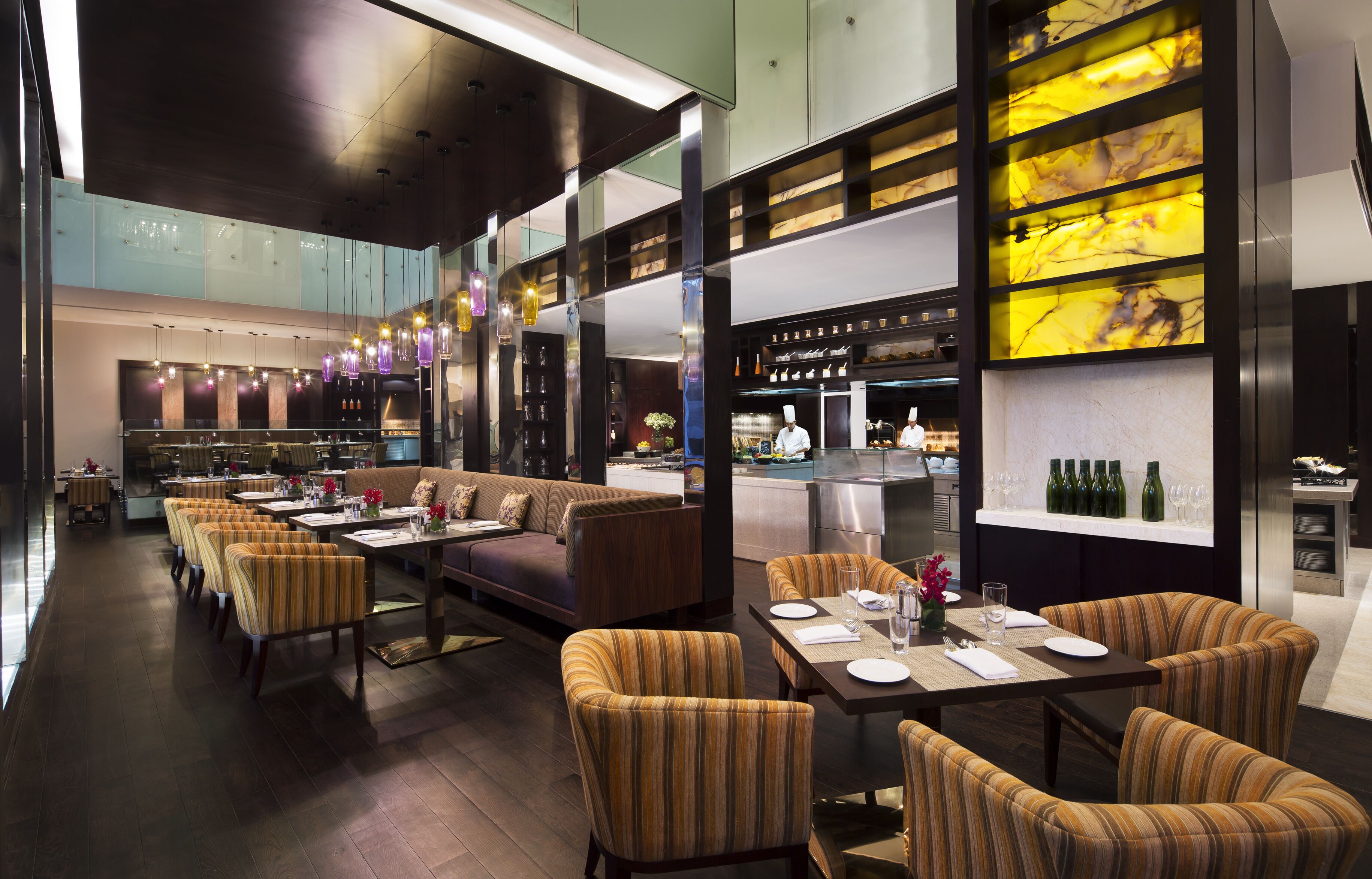Restaurante moderno com área de bar, assentos com cadeiras listradas e painel de mármore.