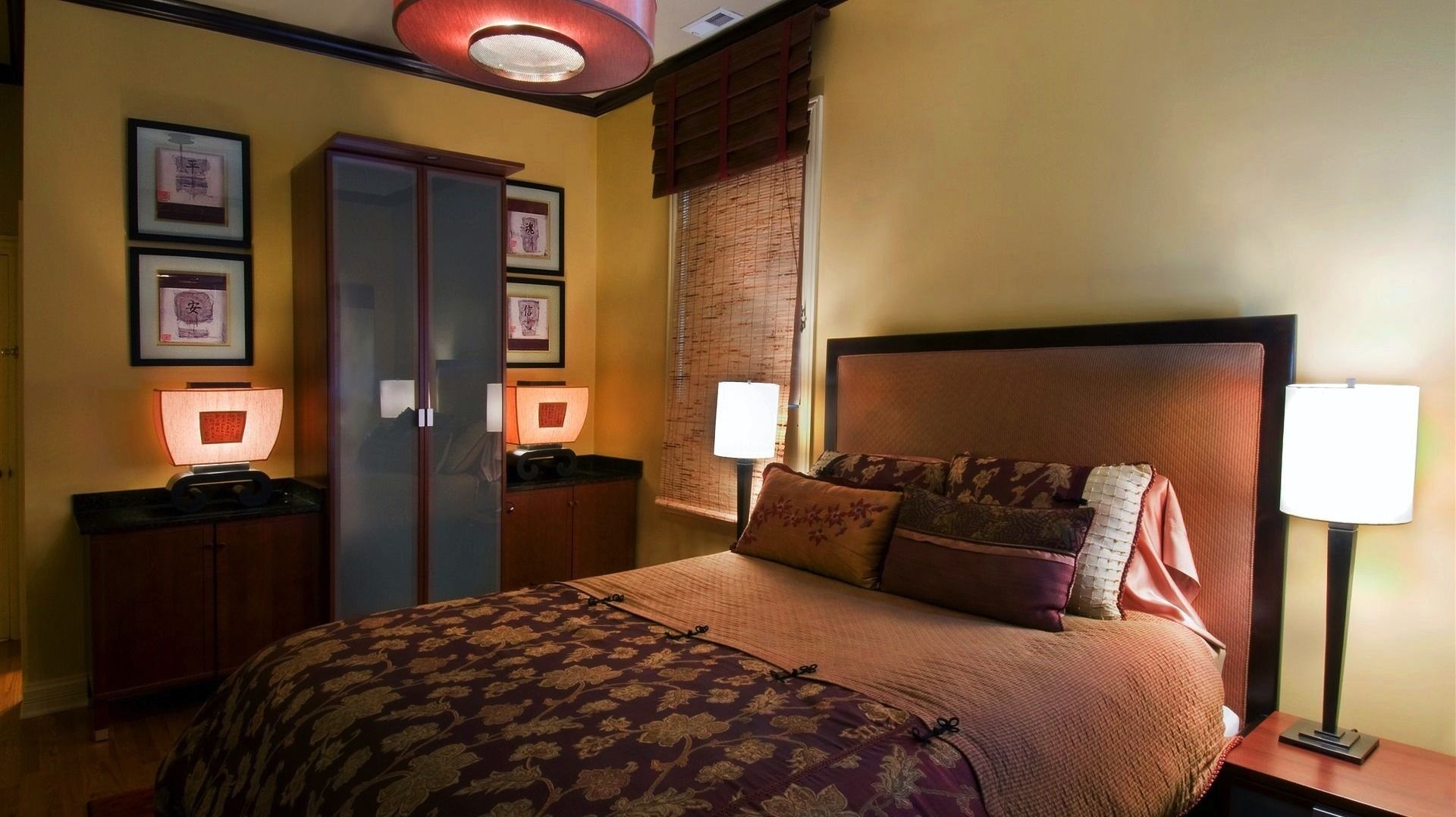 Quarto de hotel com uma cama grande, duas luminárias de cabeceira, um guarda-roupa e quadros nas paredes.