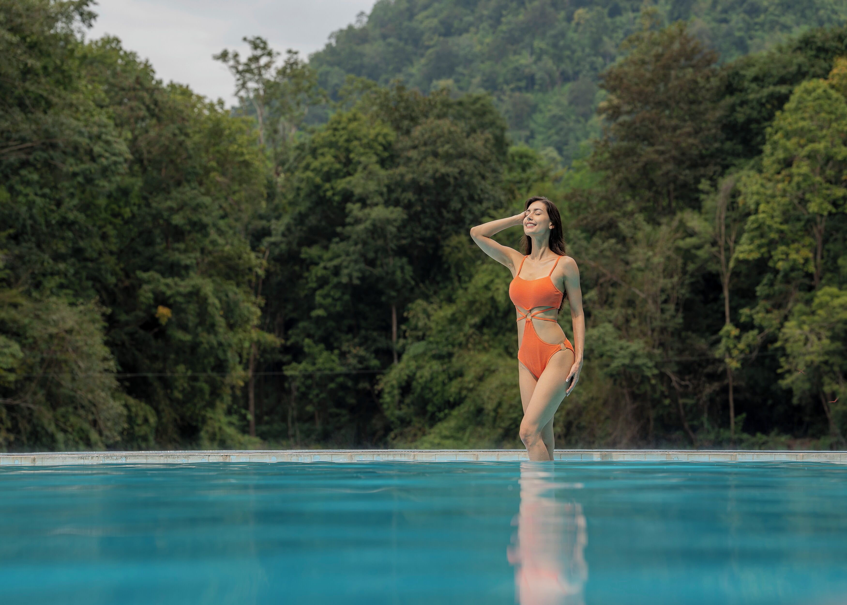 Uma pessoa de fato de banho ao lado de uma piscina, com uma área arborizada ao fundo.
