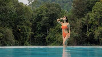 Uma pessoa de fato de banho ao lado de uma piscina, com uma área arborizada ao fundo.