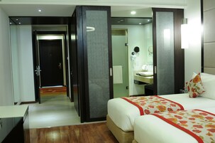 Quarto de hotel com cama, escrivaninha, banheiro e espelho.