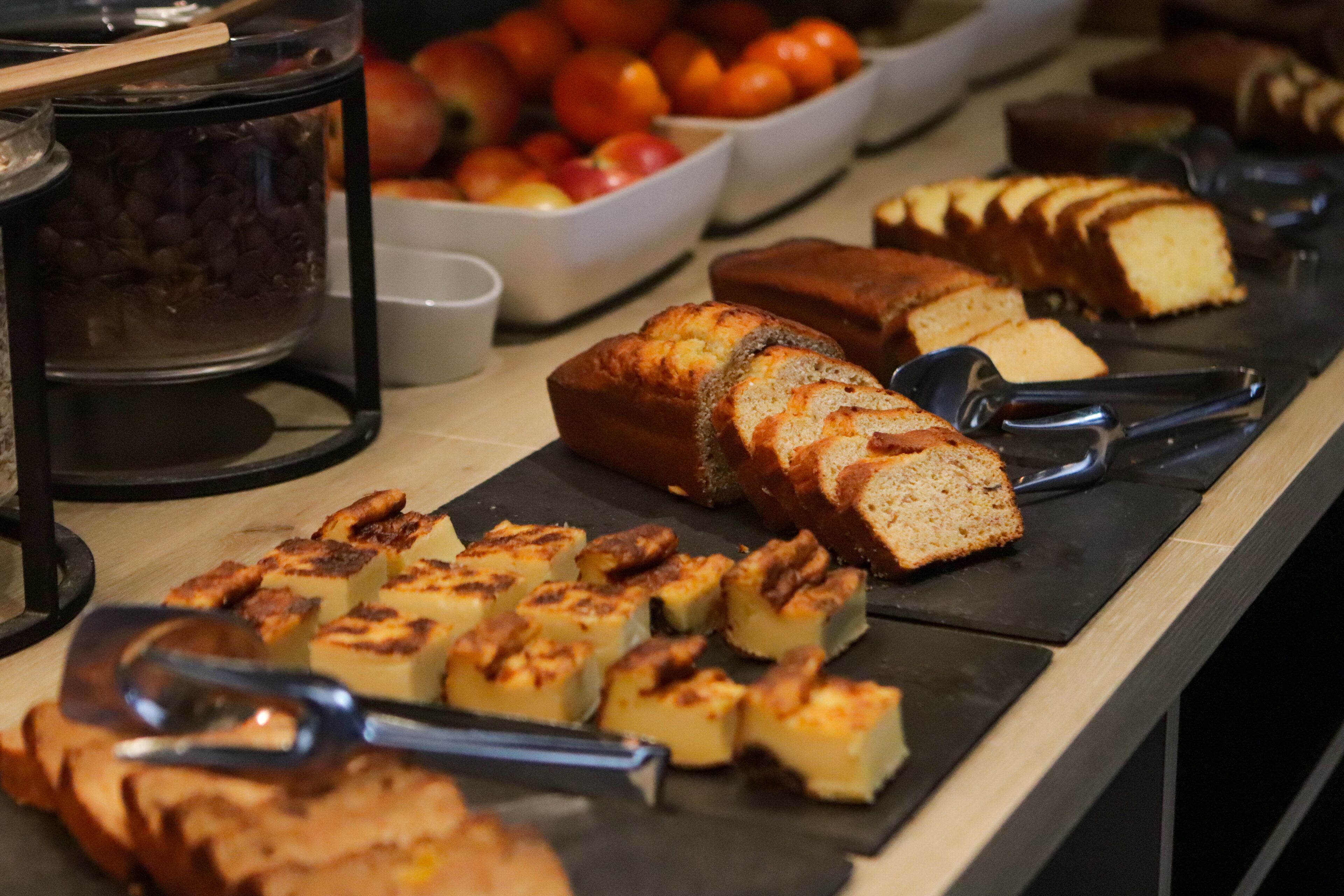 Uma mesa de buffet com diversos produtos de panificação e frutas.