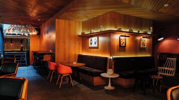Interior acolhedor de restaurante, paredes de madeira, área de bar e opções de assento, incluindo um box e mesas.