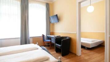 Quarto de hotel com cama, escrivaninha, cadeira, televisão e janela com cortinas.