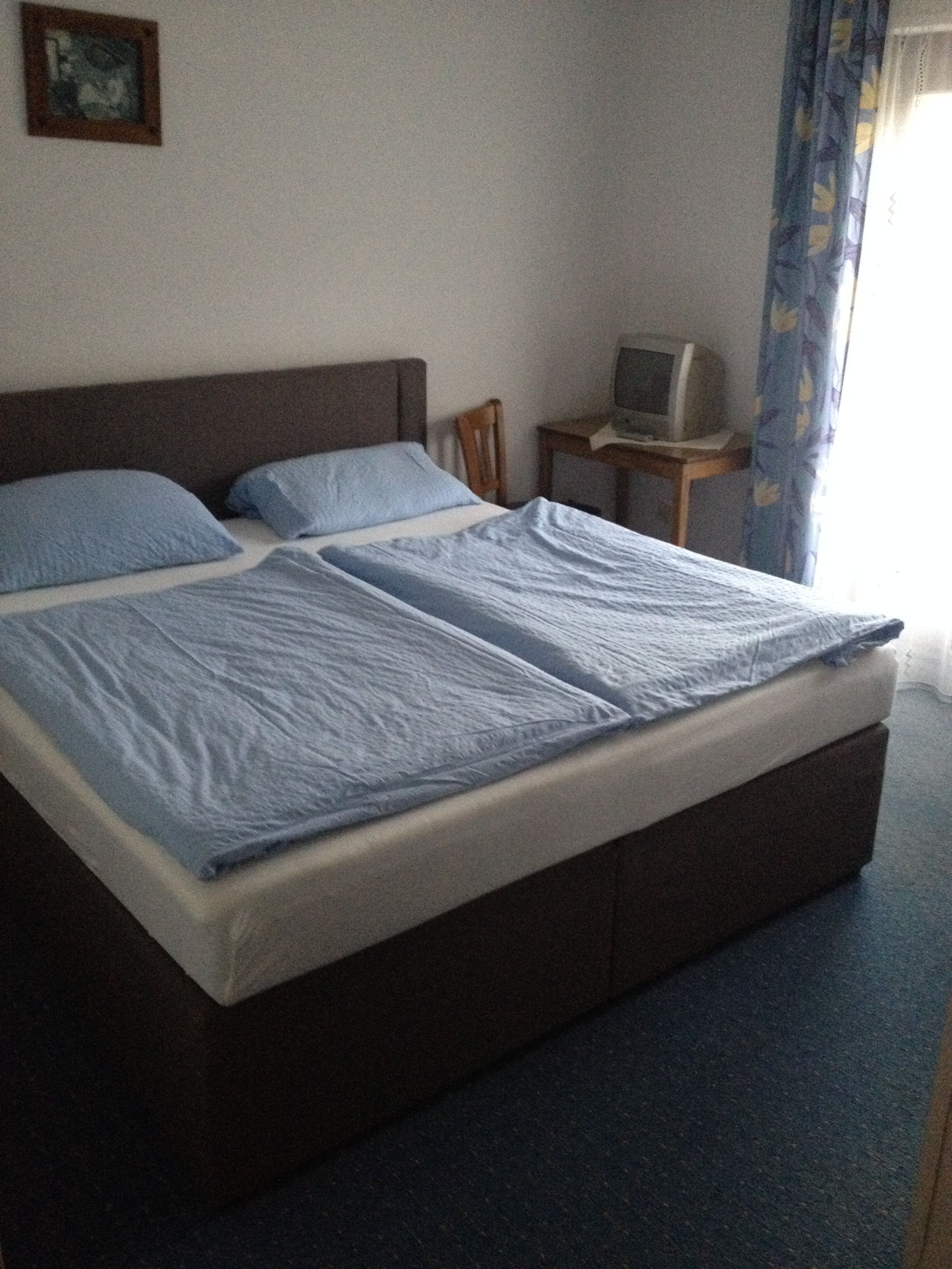 Uma cama de solteiro com cabeceira de madeira, uma pequena mesa de madeira e uma cortina azul com padrão.