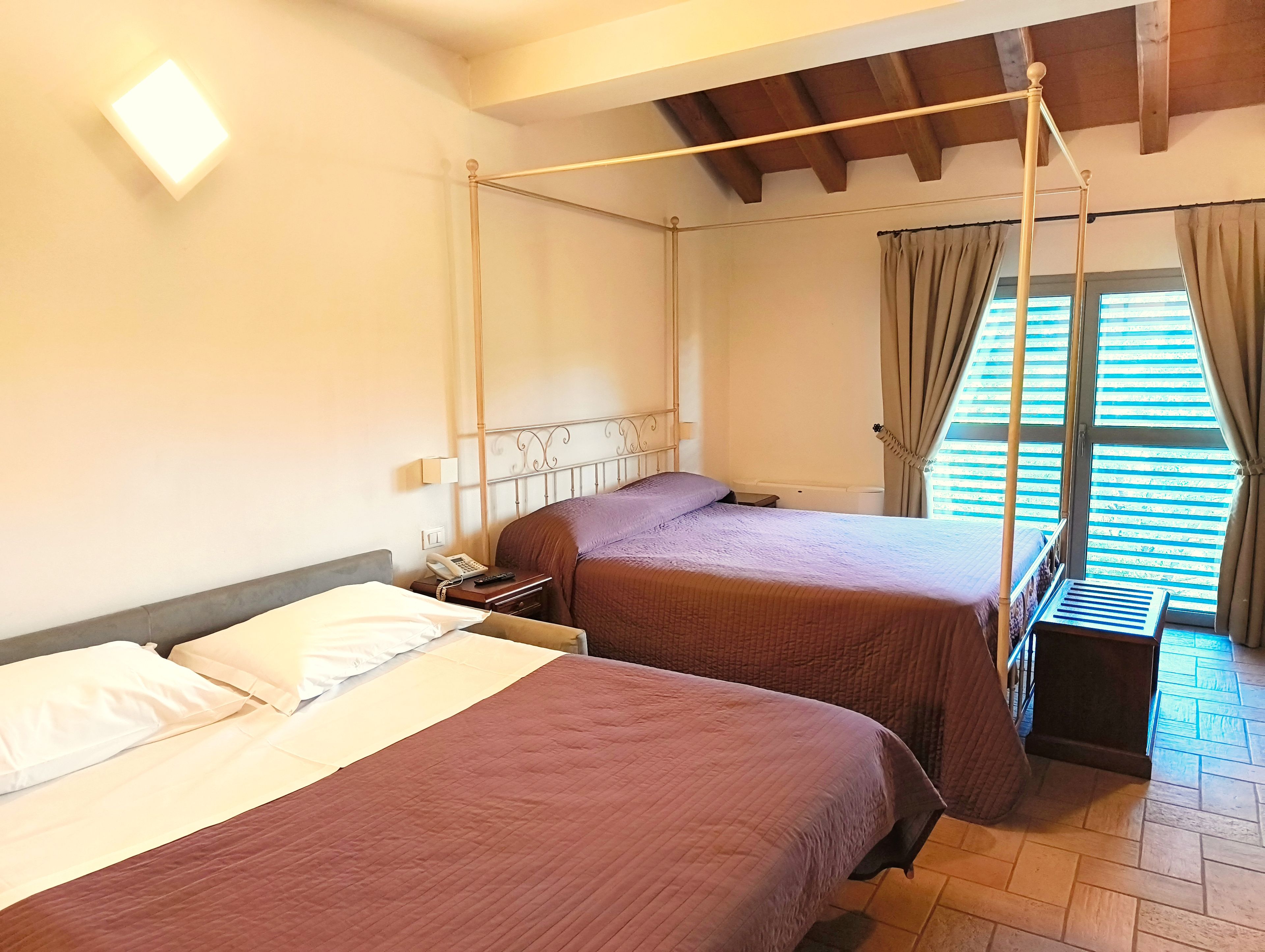 Quarto com duas camas, teto de madeira, janela com cortinas e mesa de cabeceira com telefone e controle remoto.