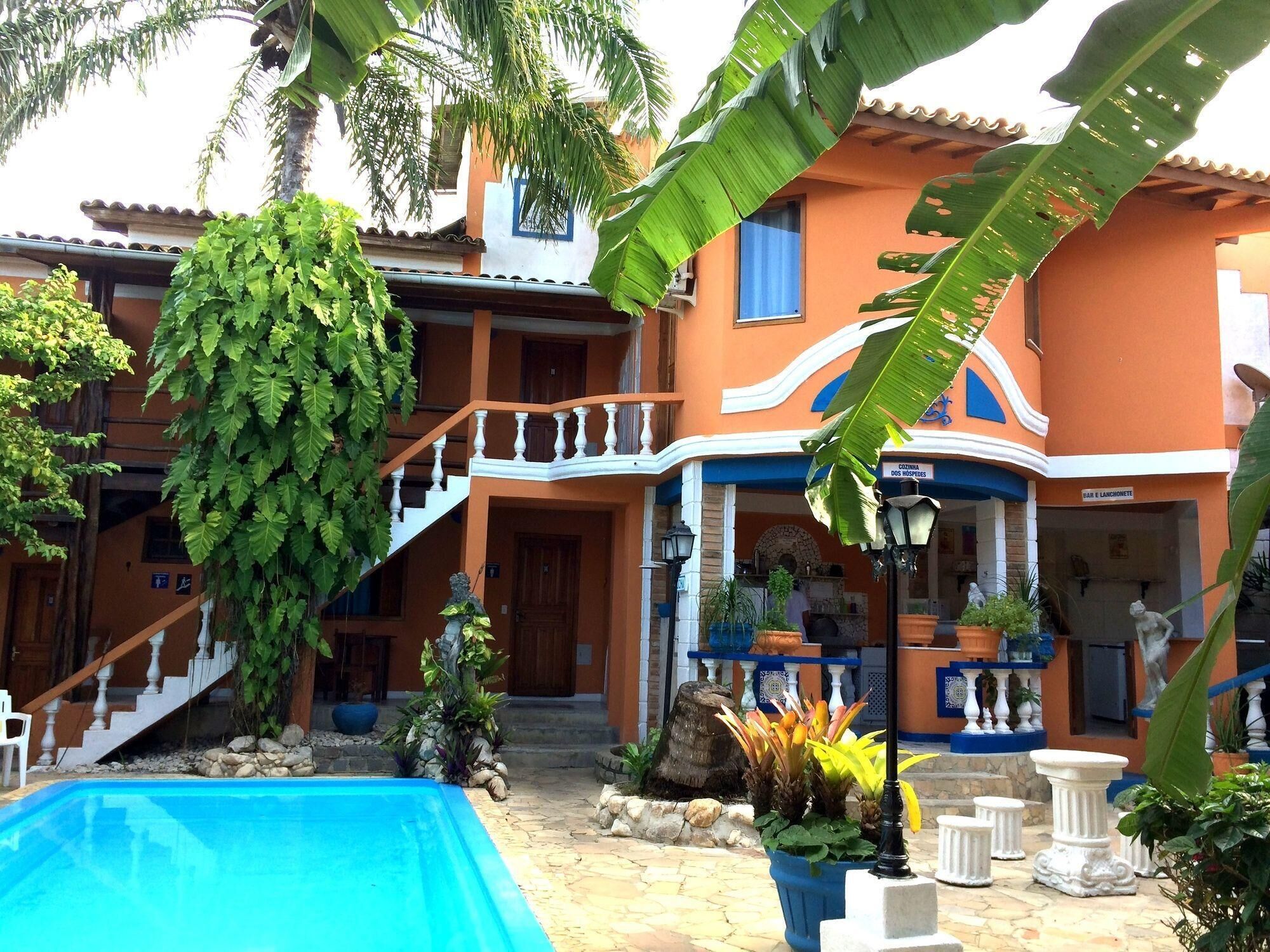 Um edifício de dois andares com piscina azul, escadaria e varanda com grades brancas.