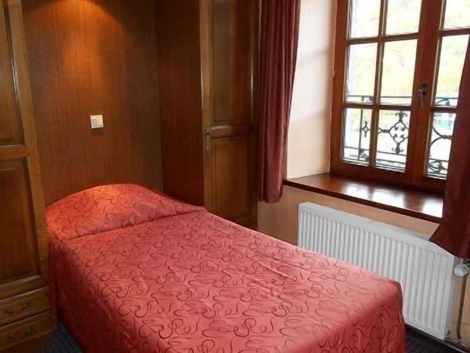 Quarto com cama, guarda-roupa de madeira, janela com cortinas e radiador.