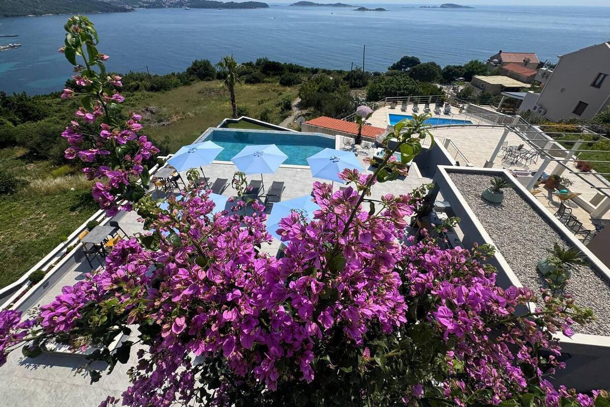 Uma área de piscina com guarda-sóis, vista para o mar e um edifício com telhado vermelho.
