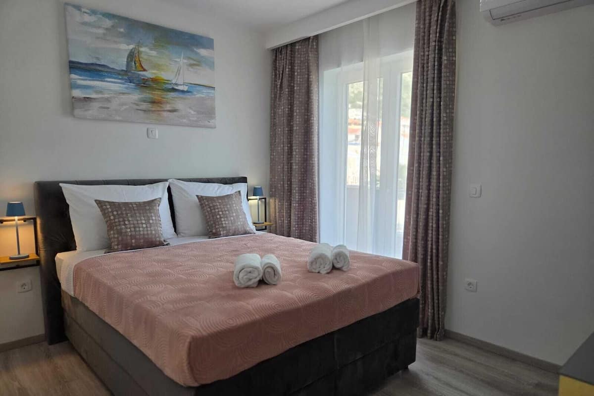 Uma cama bem arrumada com um edredom rosa, dois travesseiros e duas toalhas enroladas sobre ela.