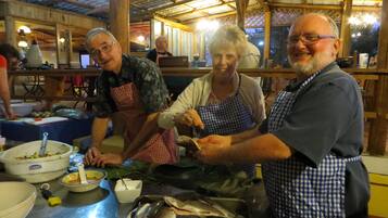 Um grupo de pessoas preparando comida em uma cozinha rústica, com vigas de madeira e teto de metal.