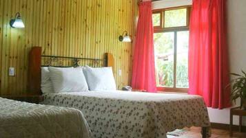 Quarto com duas camas, paredes de madeira, uma janela com cortinas vermelhas e uma pequena mesa.