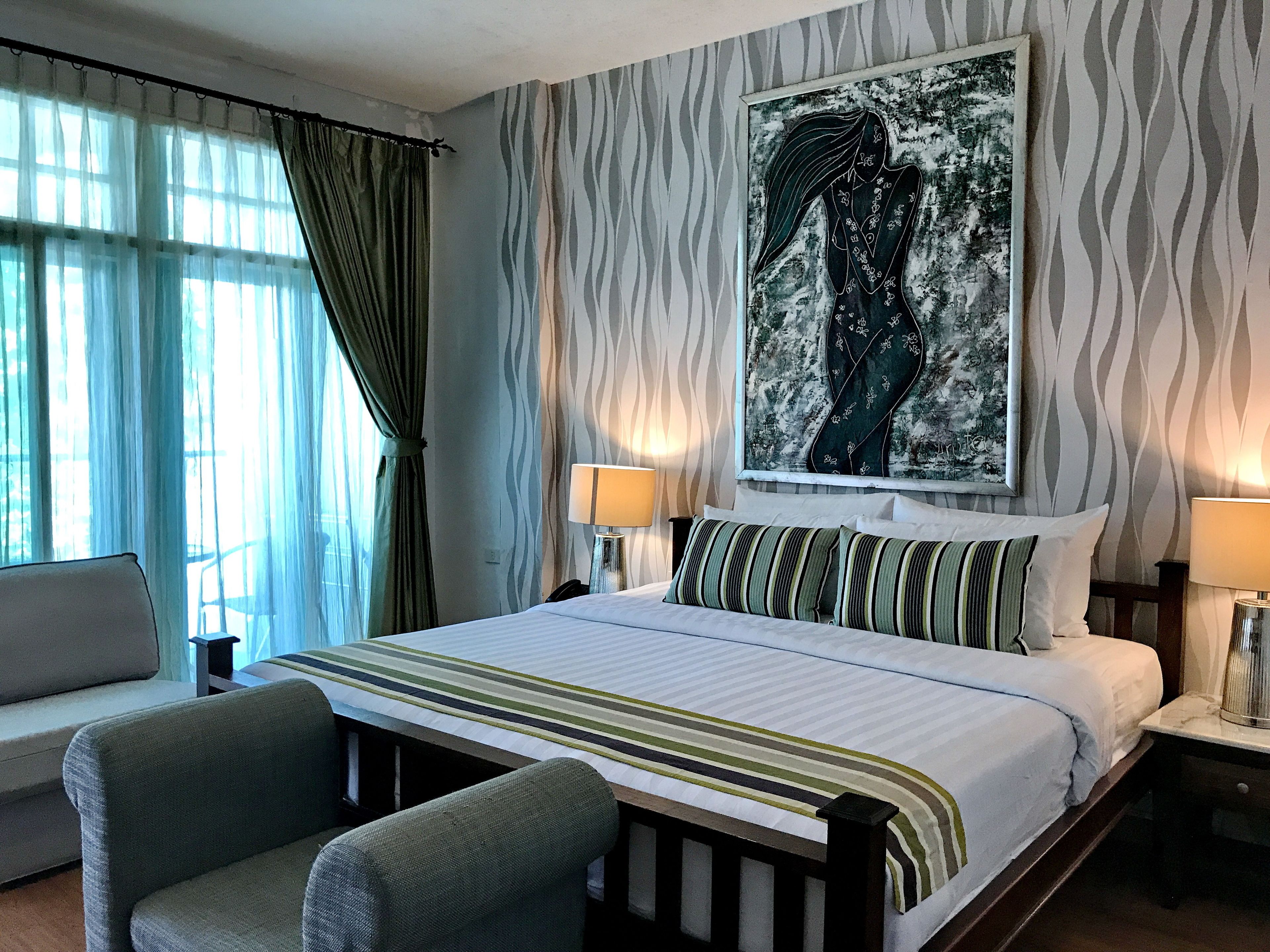 Quarto de hotel com uma cama, duas luminárias de cabeceira, um sofá e um quadro abstrato grande na parede.