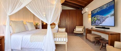 Quarto com cama de dossel, televisão e vista para a costa rochosa.