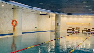 Piscina com divisórias de pista claras, um salva-vidas na parede e uma área de estar com cadeiras.