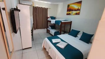 Um quarto com uma cama de solteiro, uma escrivaninha e uma cadeira. Há uma cortina, um quadro na parede e uma porta.