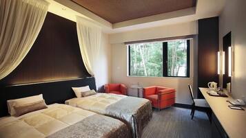 Quarto de hotel com duas camas, uma escrivaninha, uma cadeira e uma janela com vista para árvores.